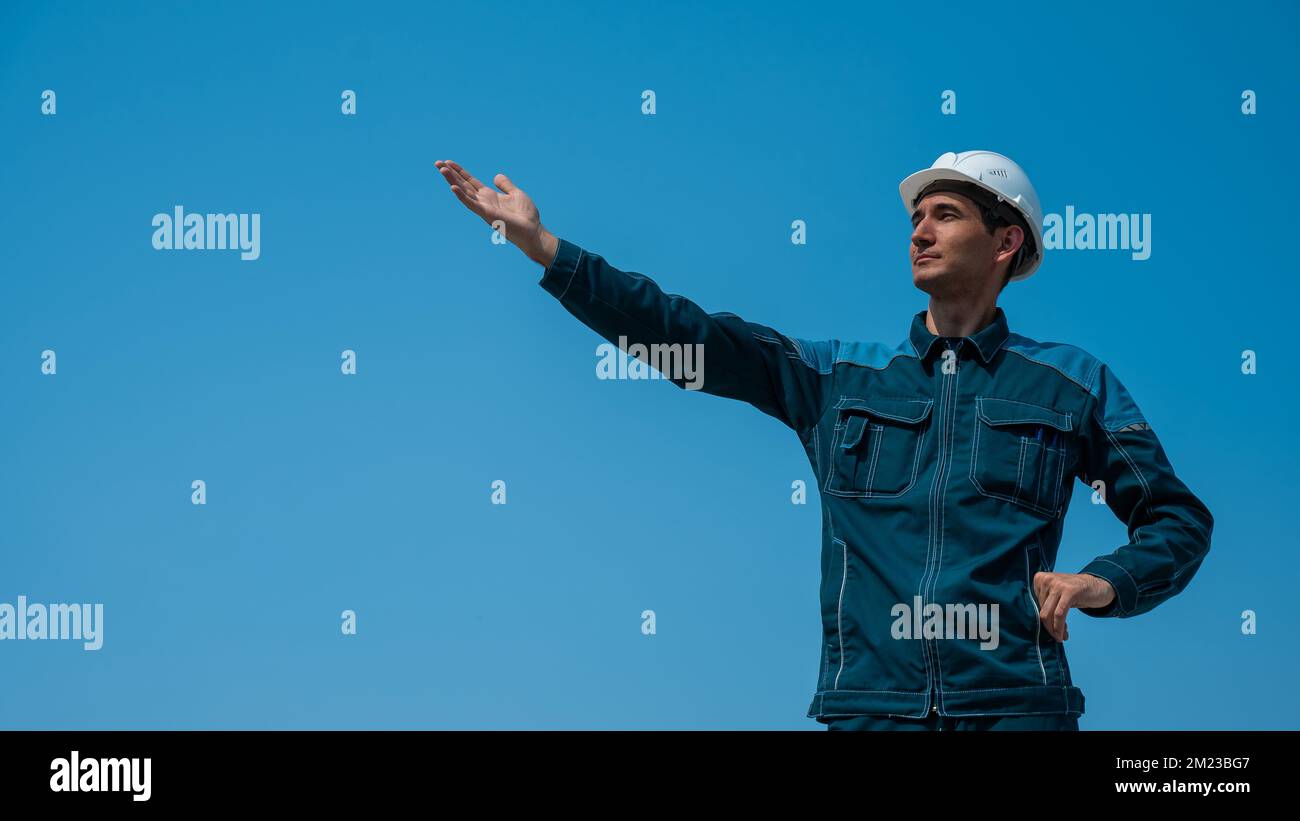 A caucasian man in work clothes and a construction helmet stands ...