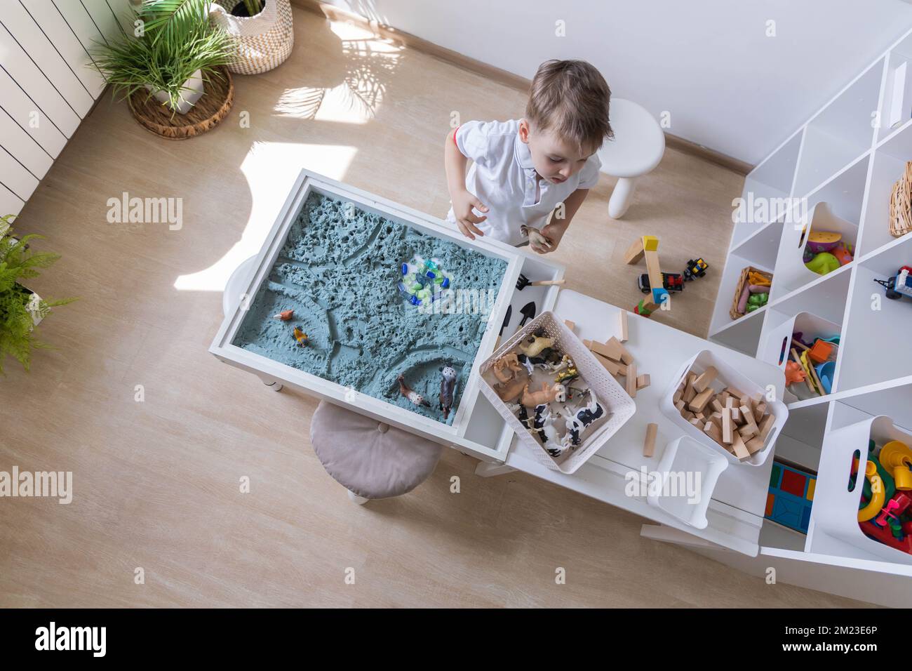 Cute baby boy playing sensory box kinetic sand table with farm animals ...
