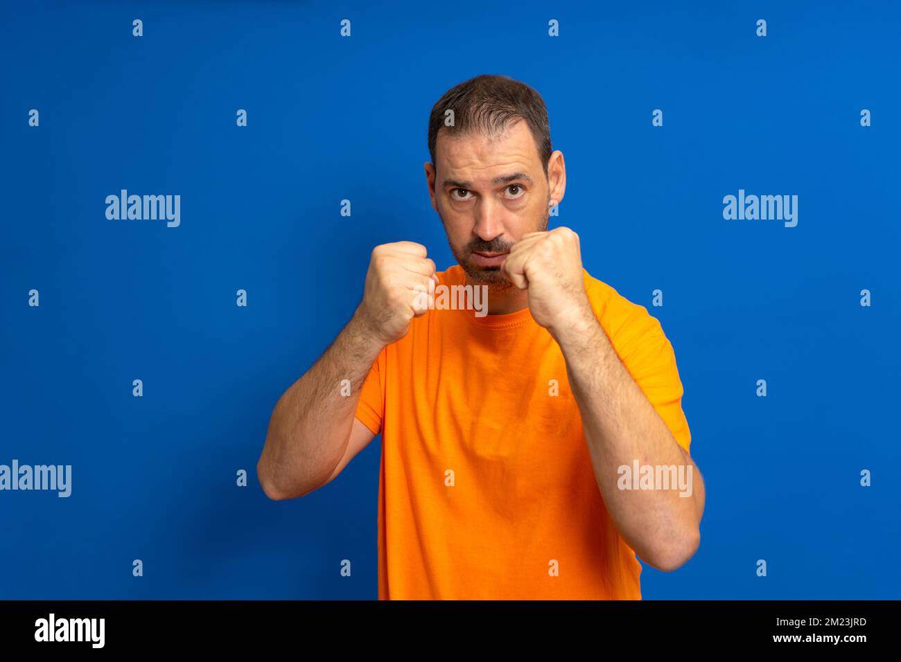Caucasian man wearing orange t-shirt over blue background ready to ...