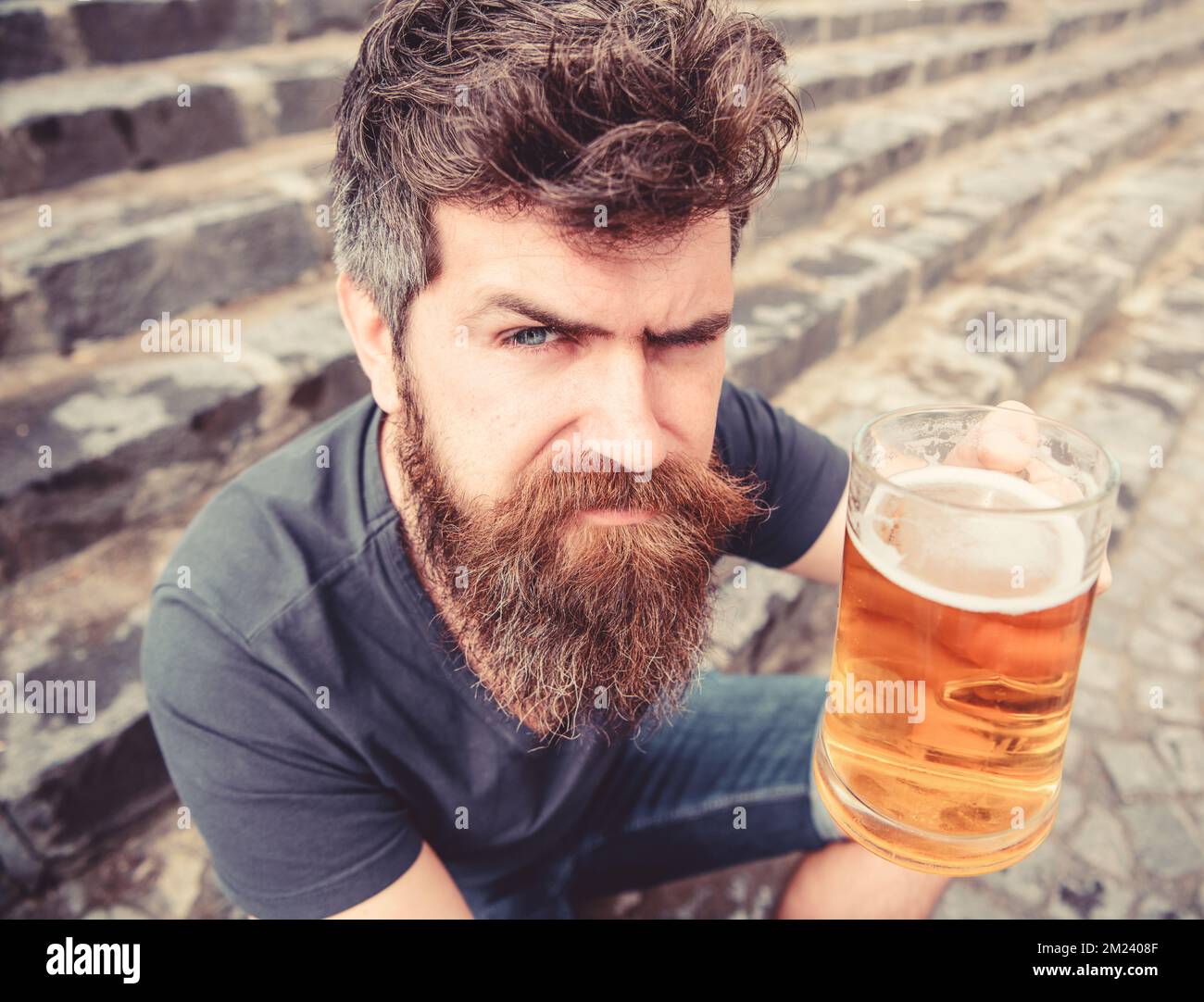 Hipster on strict face drinking beer outdoor, raising drink up. Cheers ...