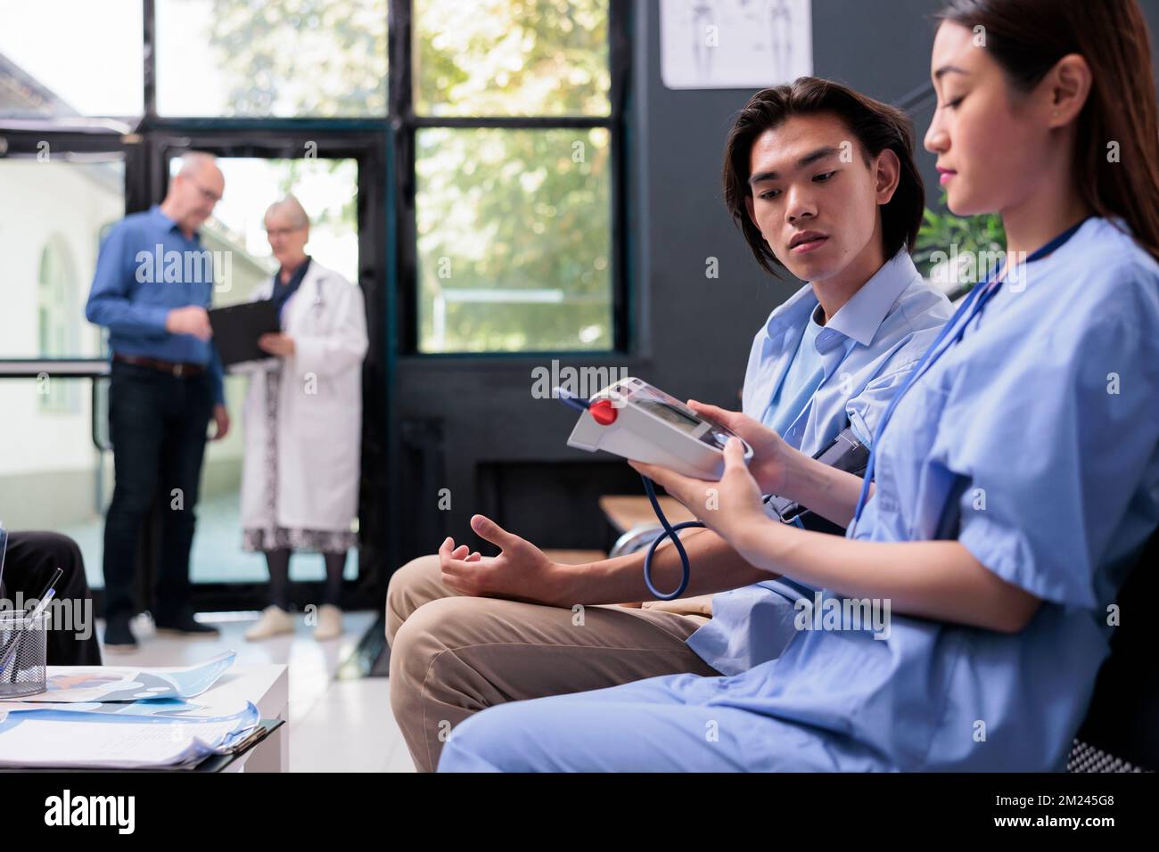 Asian medical assistant measuring patient blood pressure and ...