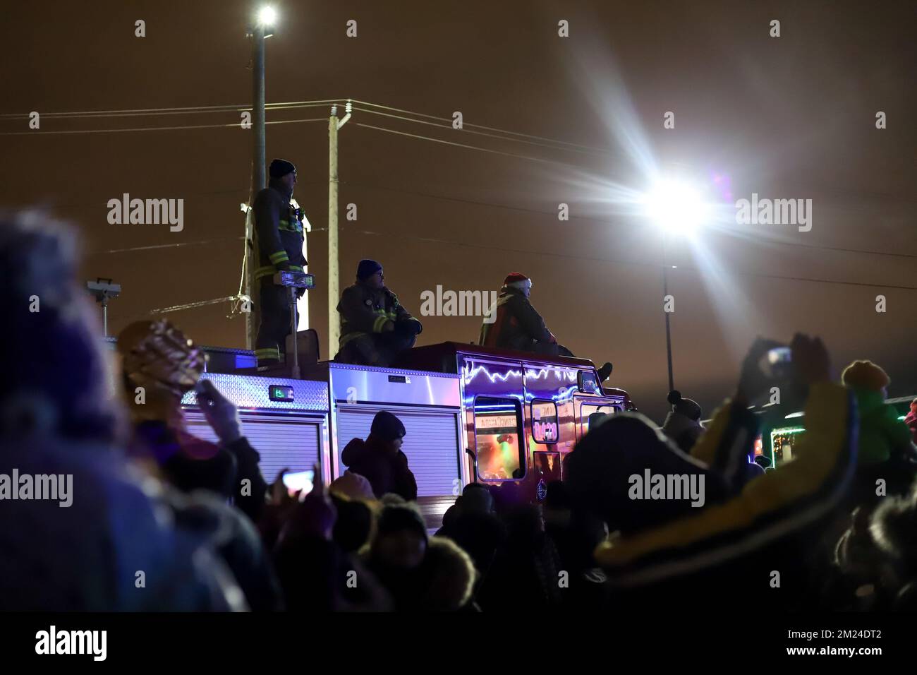 A crowd of people and firefighters on a fire truck watch the arrival of ...