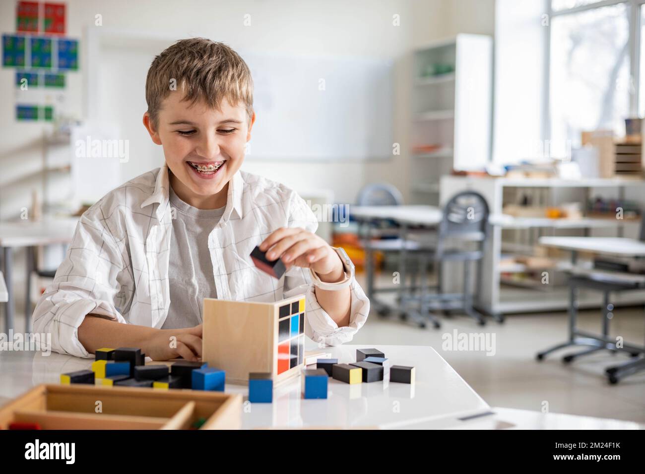 Happy male kid assembling Montessori material trinomial cube at school ...