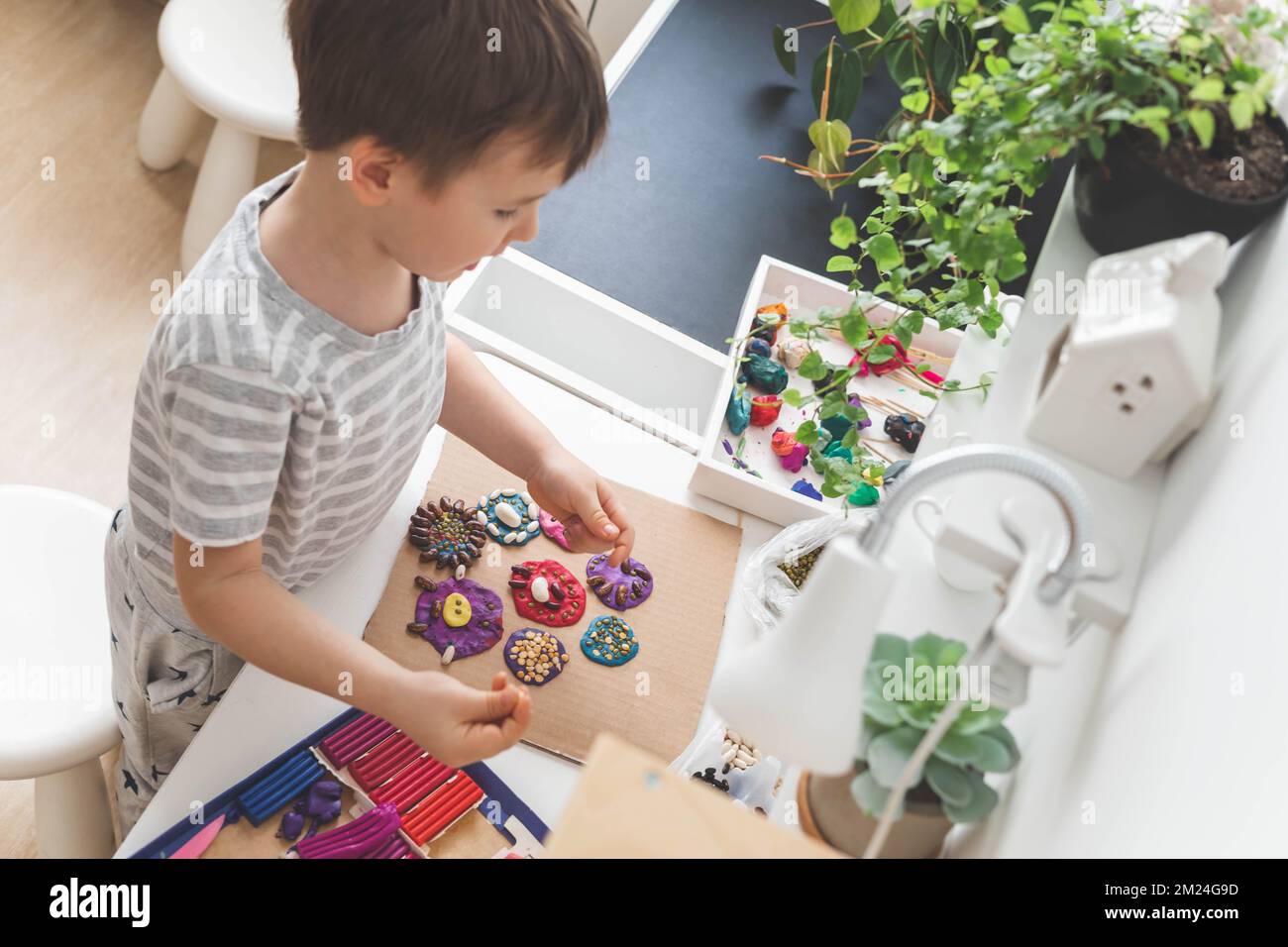 Baby boy creating plasticine diy figure with decorate dried beans ...