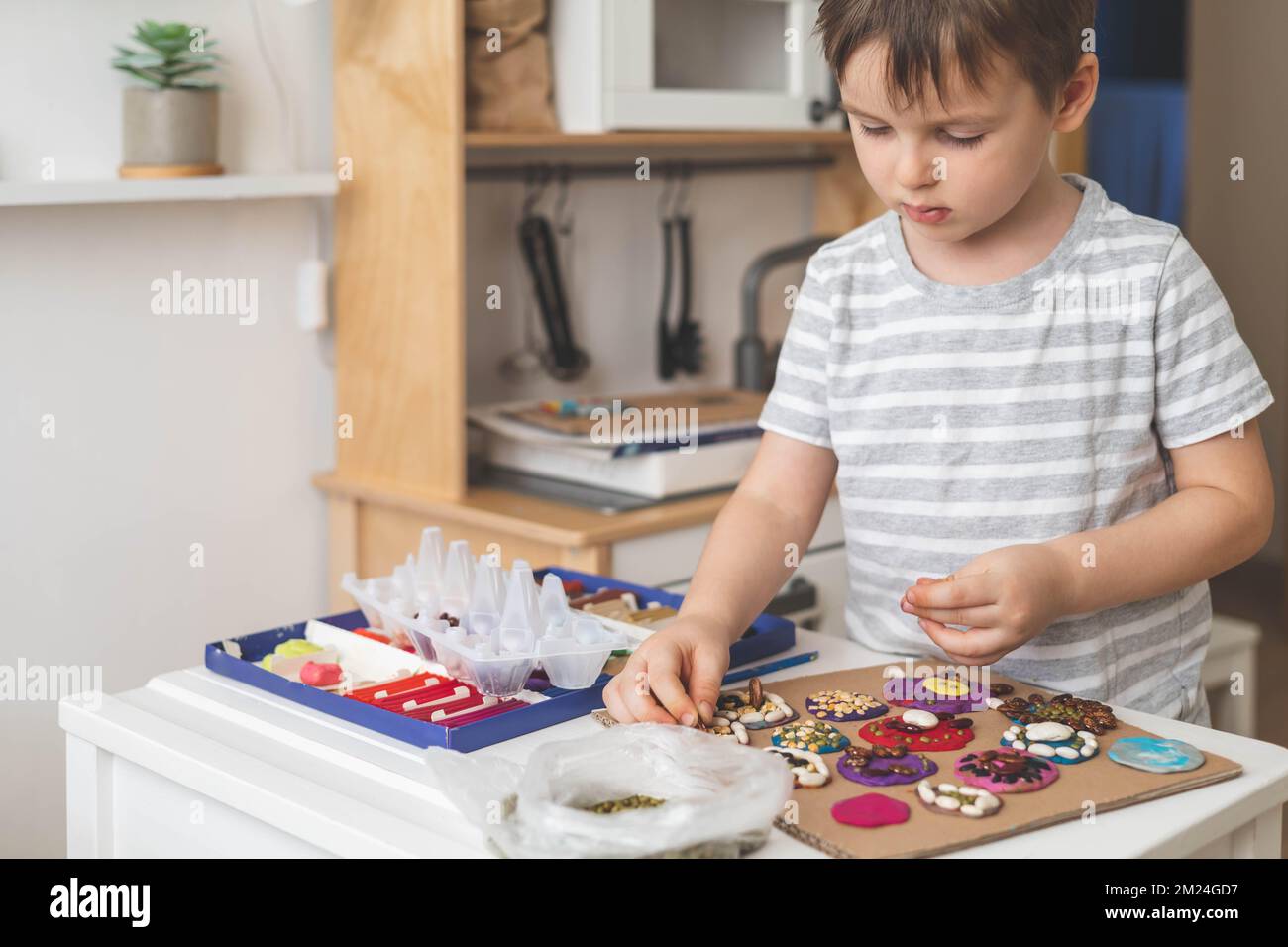 Baby boy creating plasticine diy figure with decorate dried beans ...