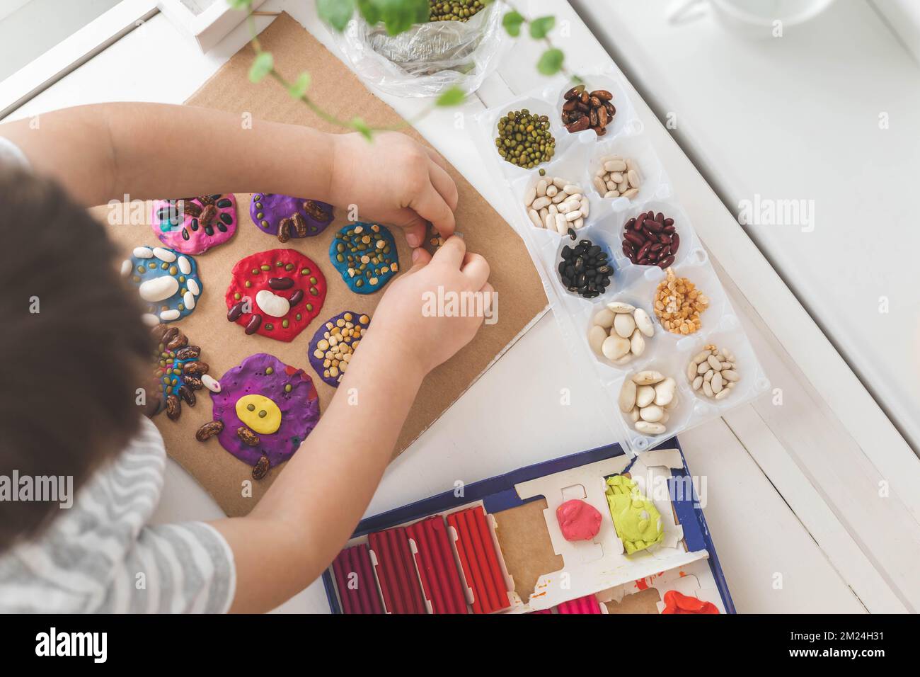 Baby boy creating plasticine diy figure with decorate dried beans ...