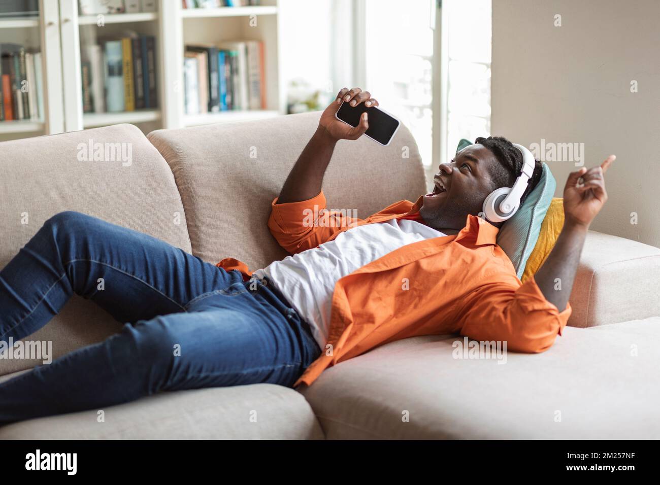 Joyful black guy reclining on sofa, singing songs Stock Photo - Alamy