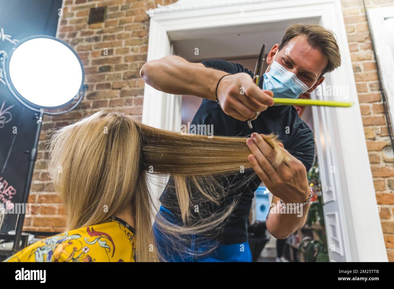 Male hairdresser in protective mask cutting hair of a woman with ...