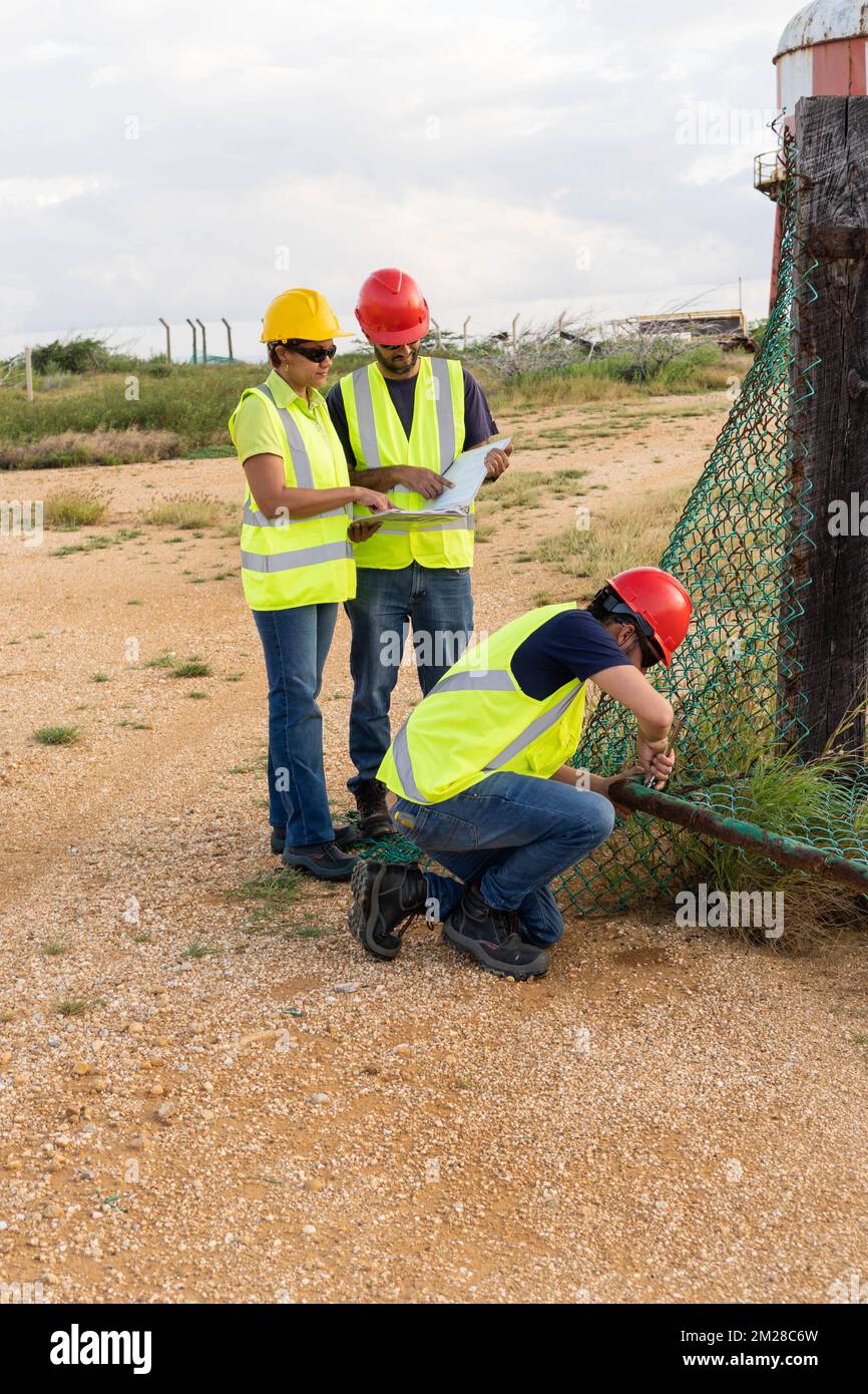 Three industrial workers at work in front of a refinery Stock Photo - Alamy
