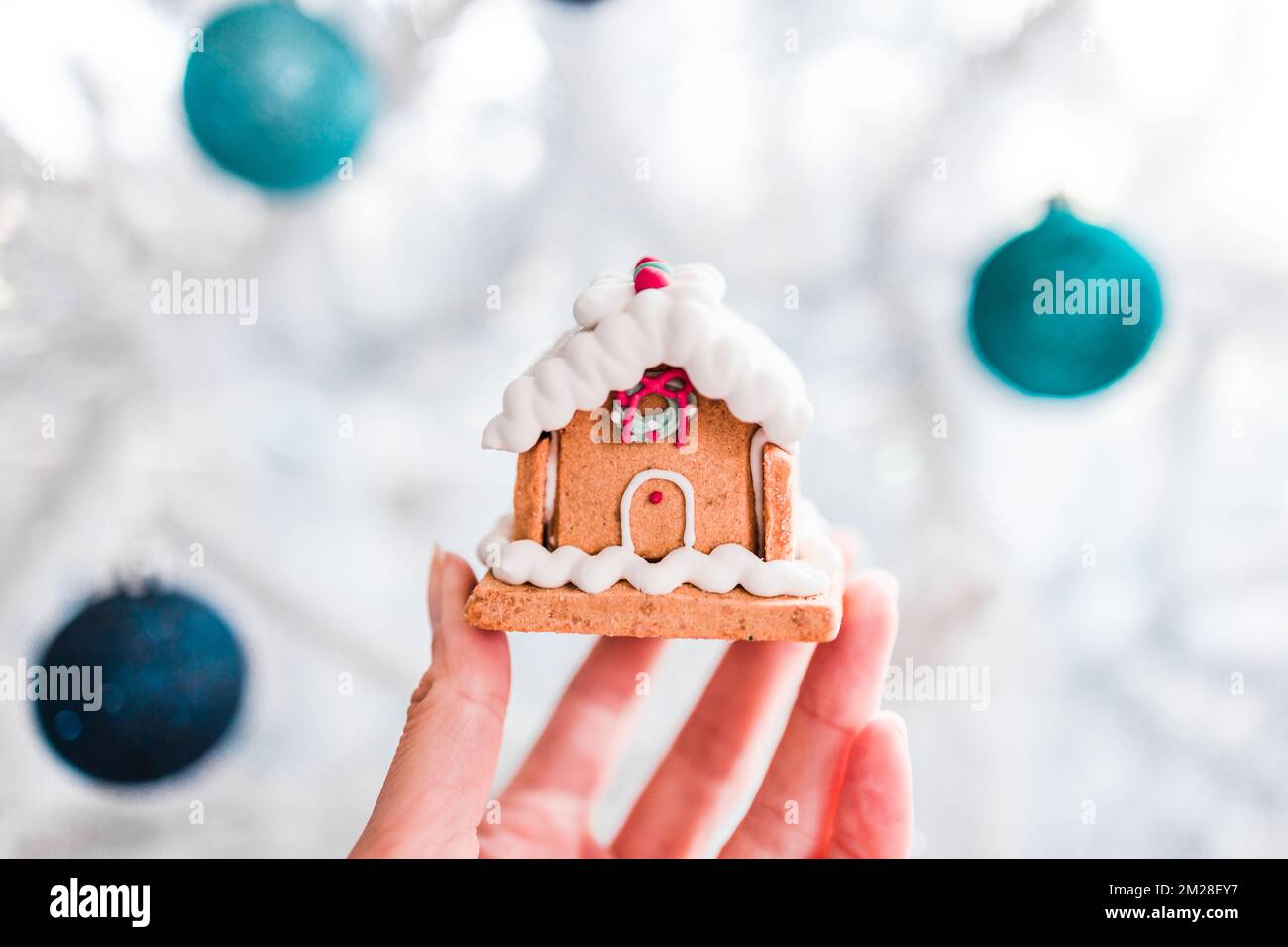 gingerbread house in front of snowy Christmas tree with white and blue ...