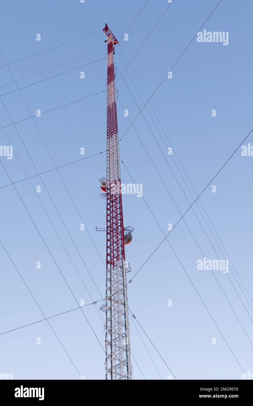 tall wireless communications tower tethered by cables against blue sky ...