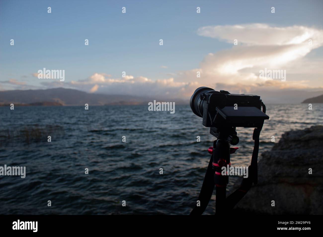 Close up to a modern camera over a tripod with blue lake, mountains and ...