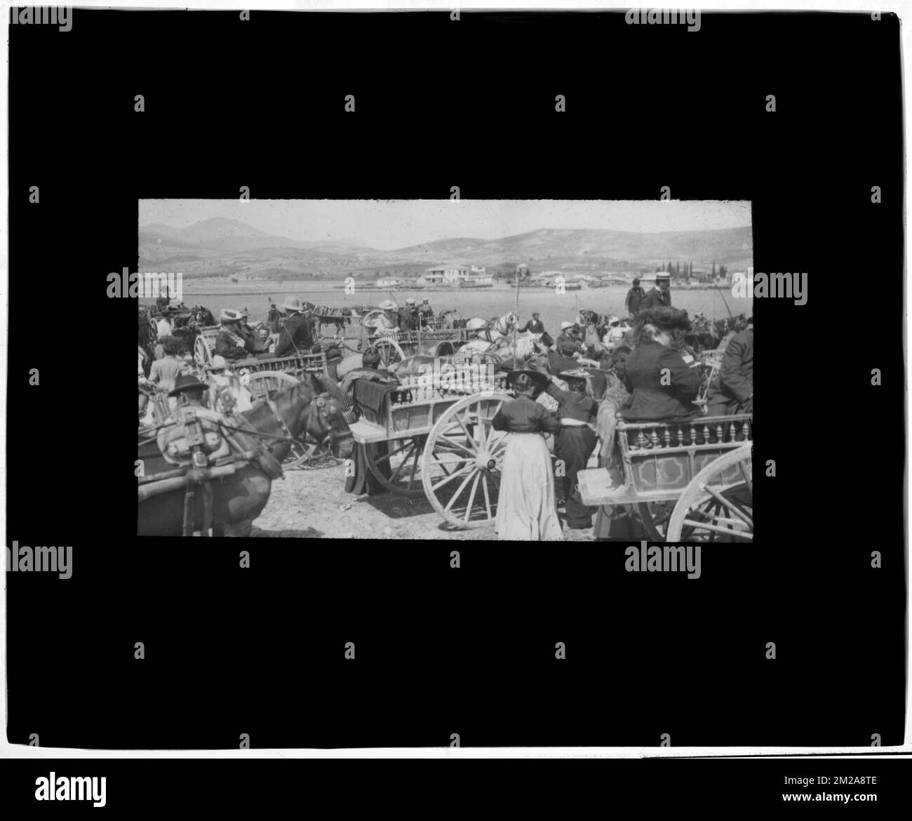 Cluster of people and horse-drawn carriages gathered by water ...