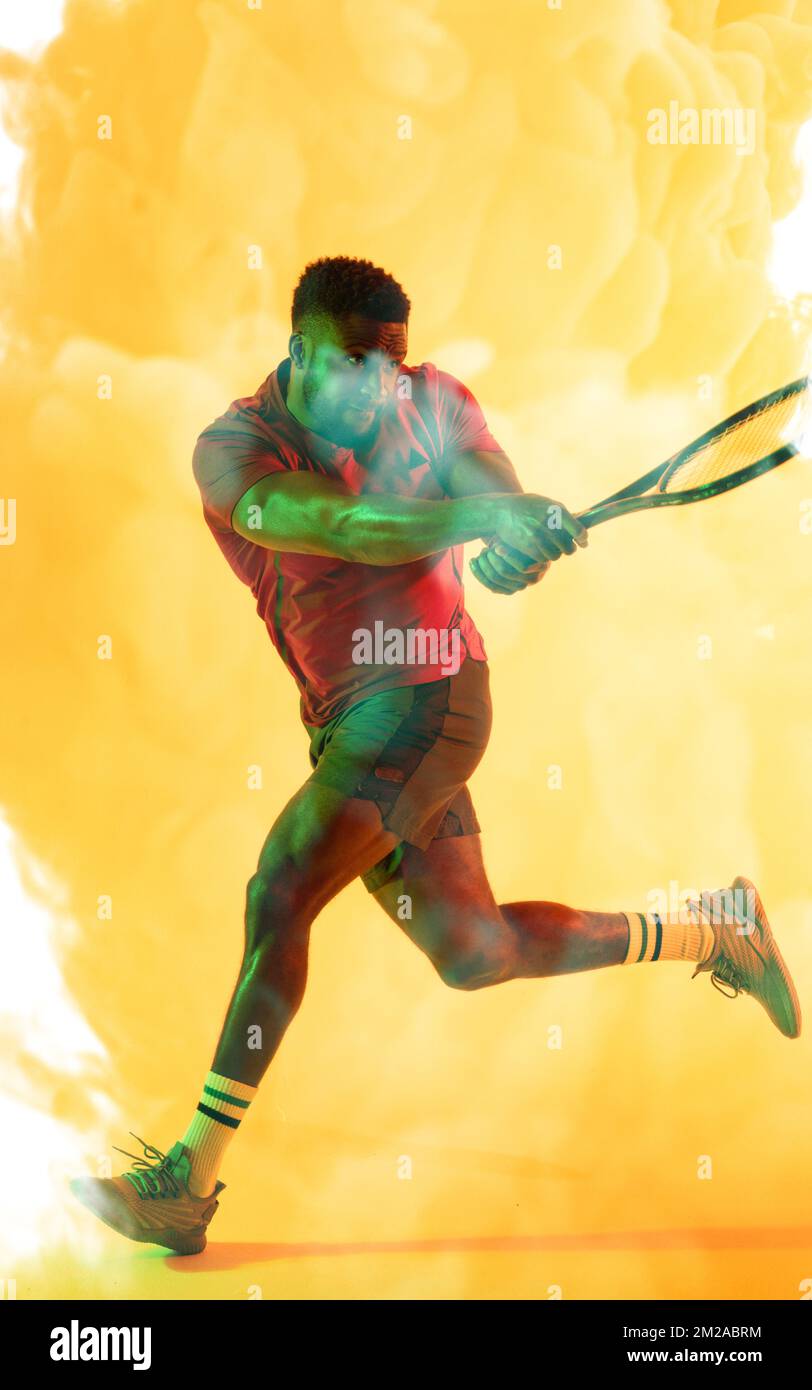 African american male tennis player hitting with racket against smoky ...