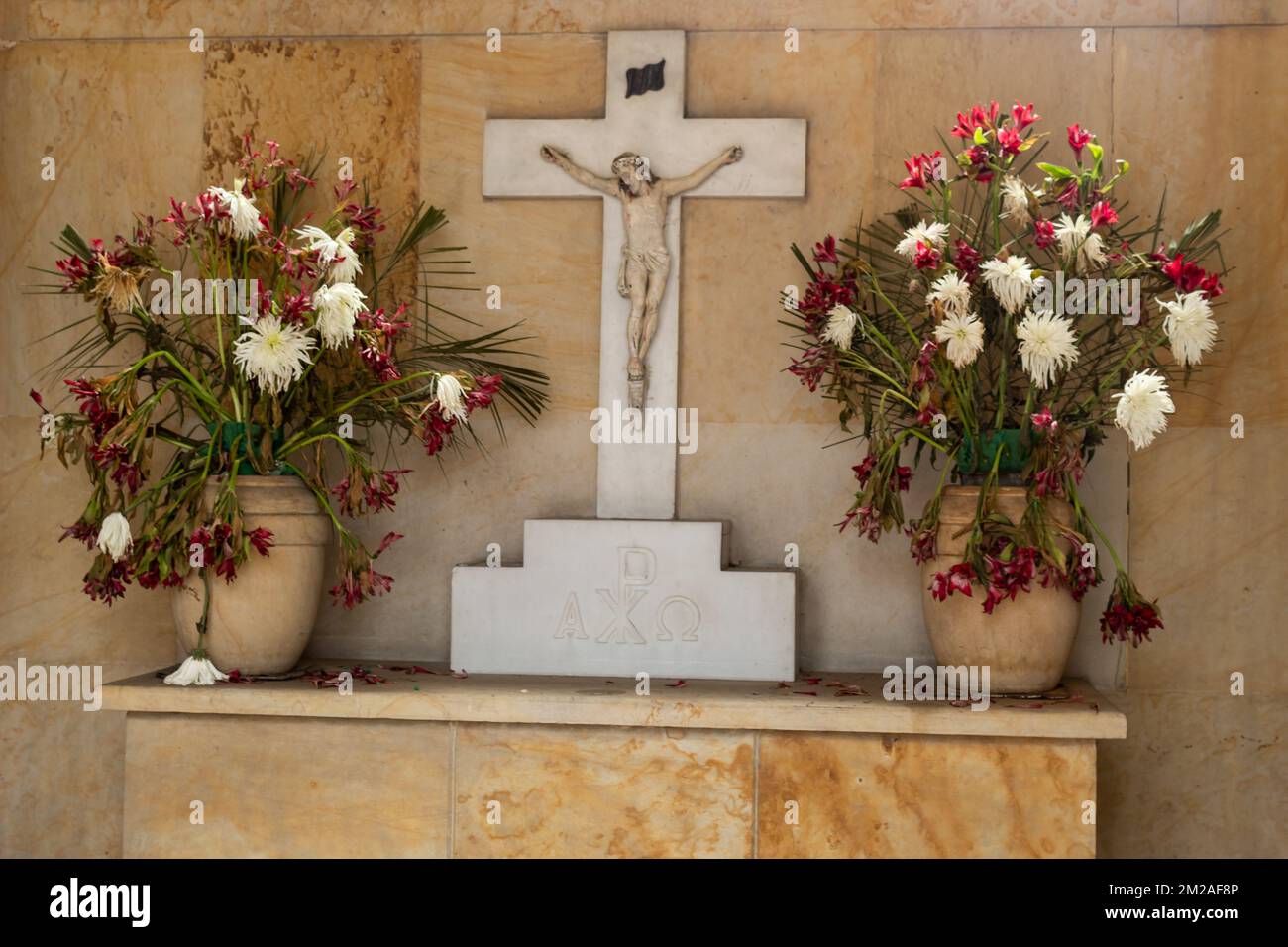 Crucified Jesus Christ figure in altar with withered white and red flowers in marble background ...