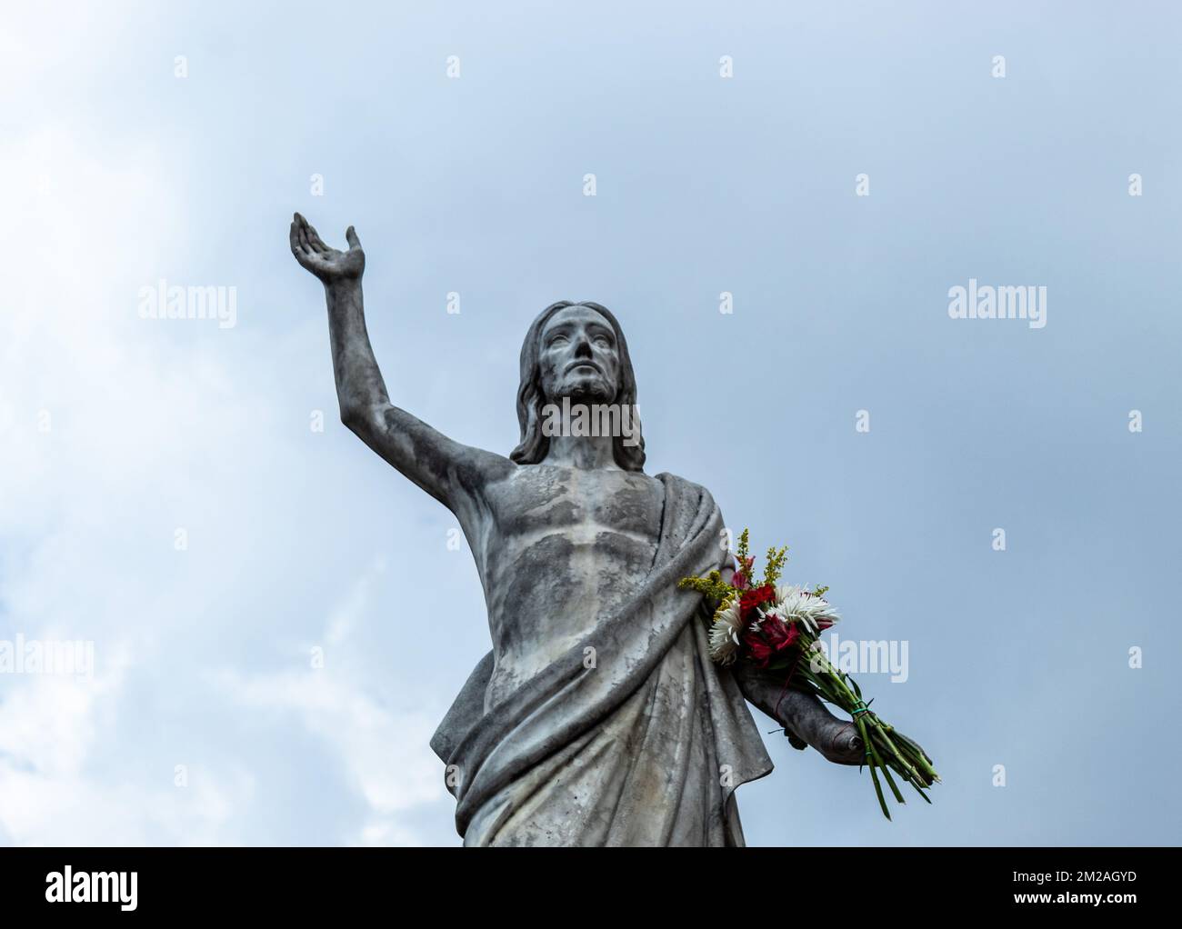 An old Jesus Christ resurrected statue with a multicolor bouquet ...