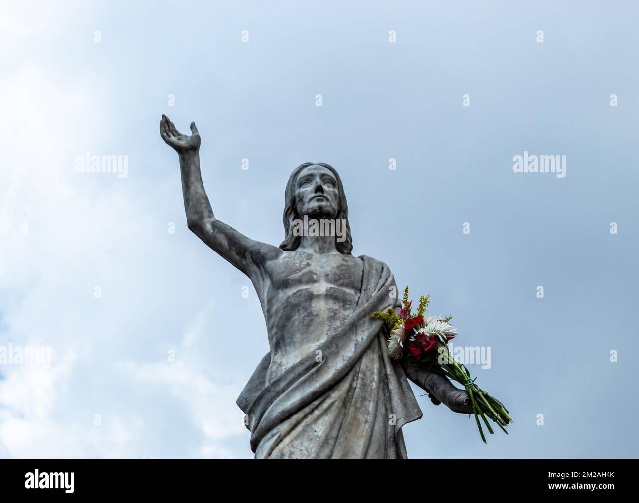 An old Jesus Christ resurrected statue with a multicolor bouquet ...