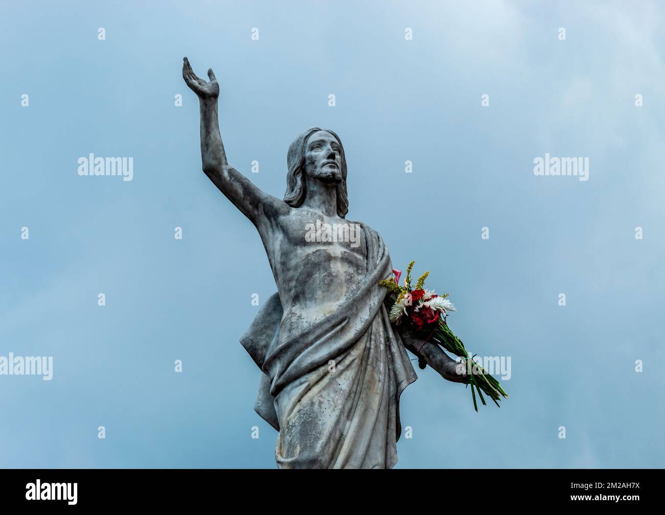 An old Jesus Christ resurrected statue with a multicolor bouquet ...