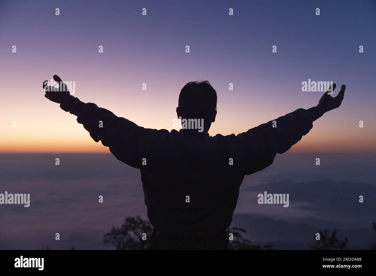 Silhouette of a young man praying to God on the mountain at sunset ...
