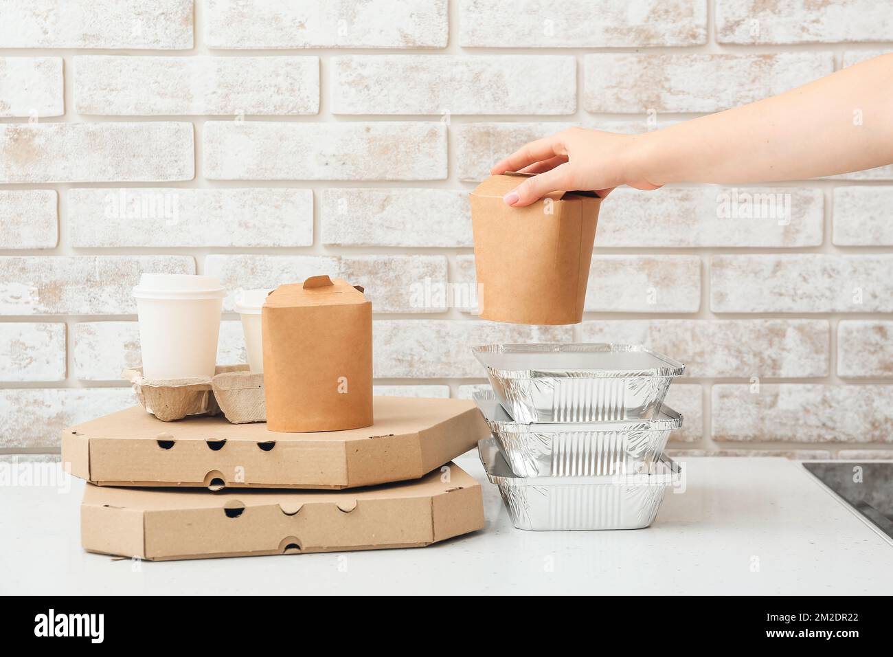 Female hand with box and set of food delivery containers on white table ...