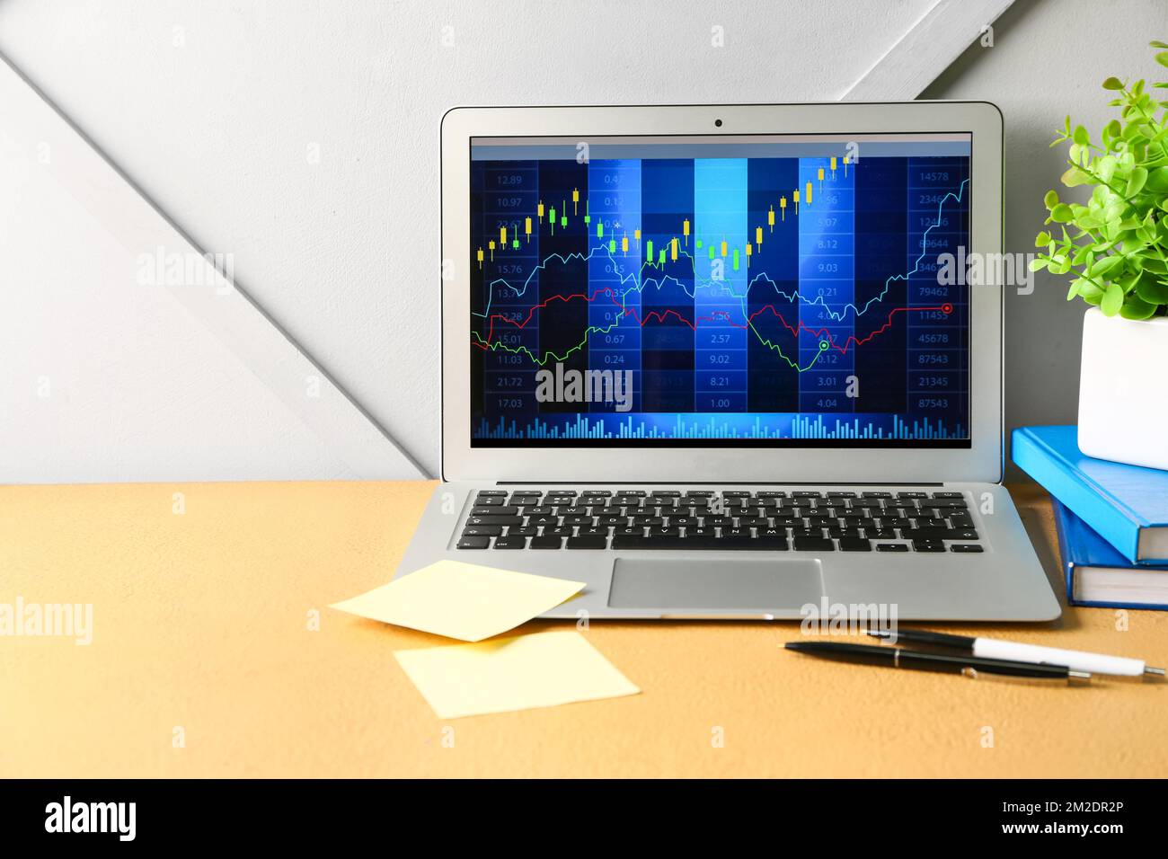 Laptop with trading charts and sticky notes on table near light wall ...