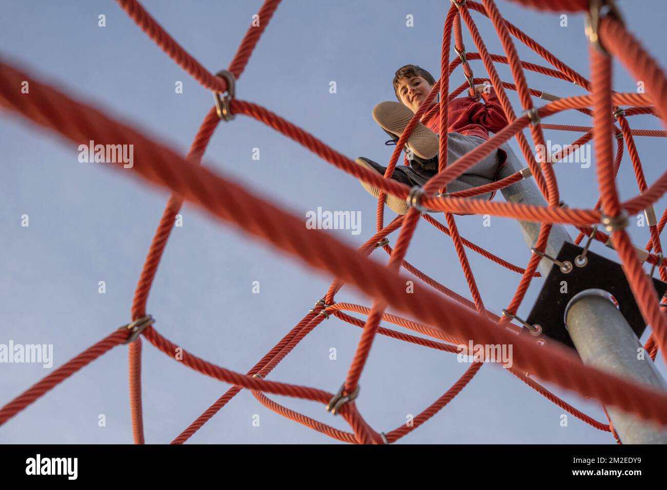 kid on the top looking down after climbing the ropes in a playground ...