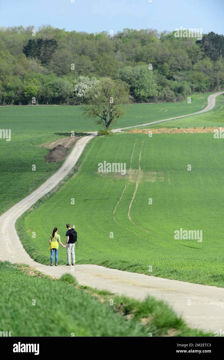 Couple of hikers walking on a small countryside road and holding a ...
