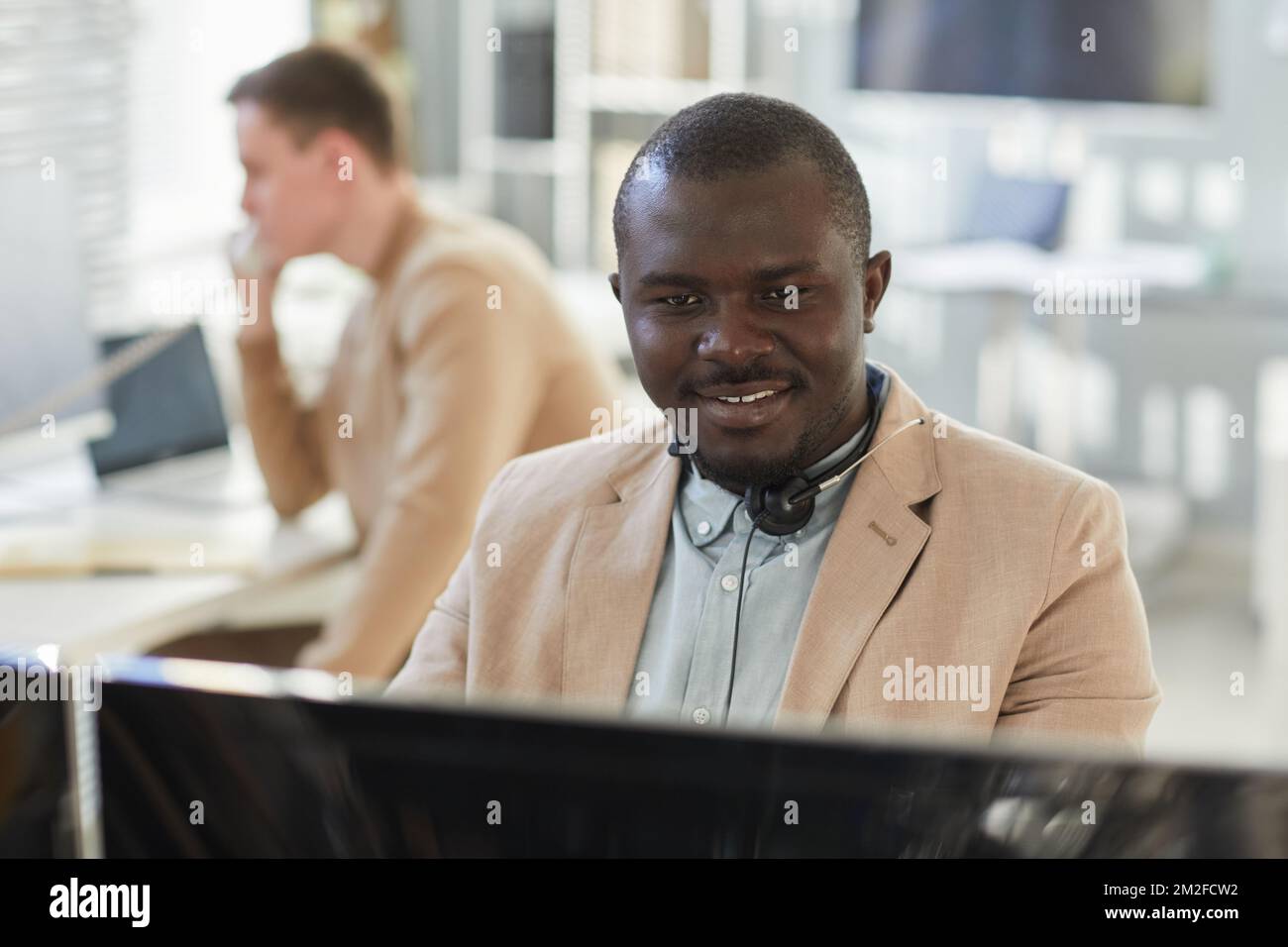 Portrait of smiling black man looking at computer screen while working ...