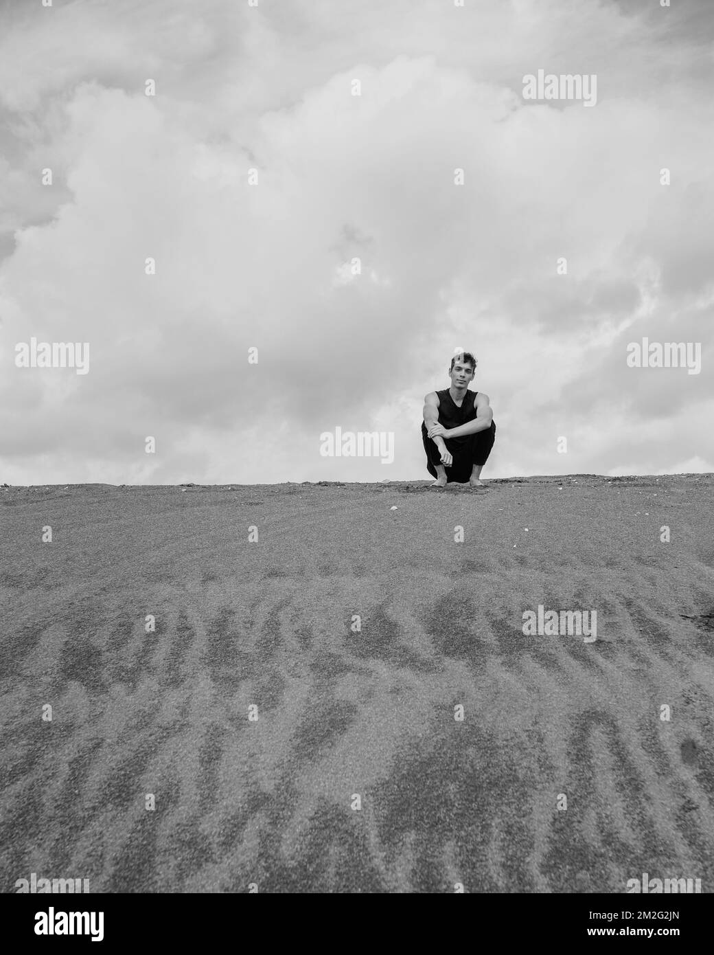 Lone man sitting barefoot on the sand in sandy desert on the horizon ...
