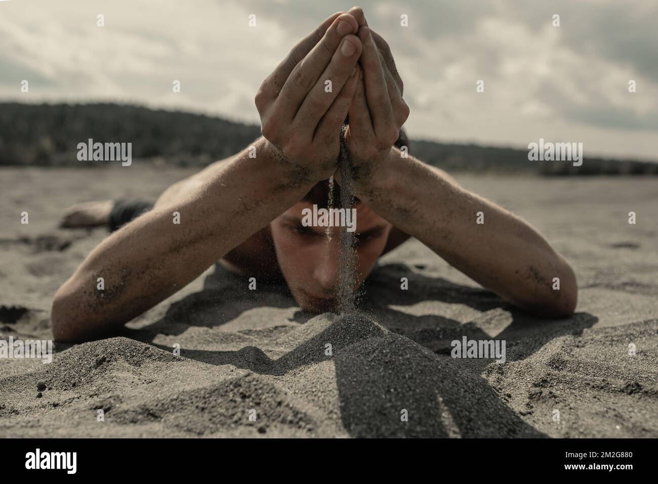 Man lying on his stomach and pouring sand through hands in the desert ...