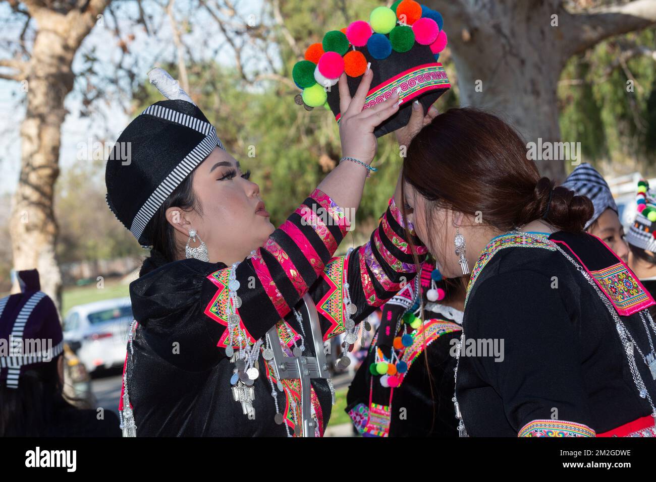 A young woman in traditional attire places a pom pom hat on her friend ...
