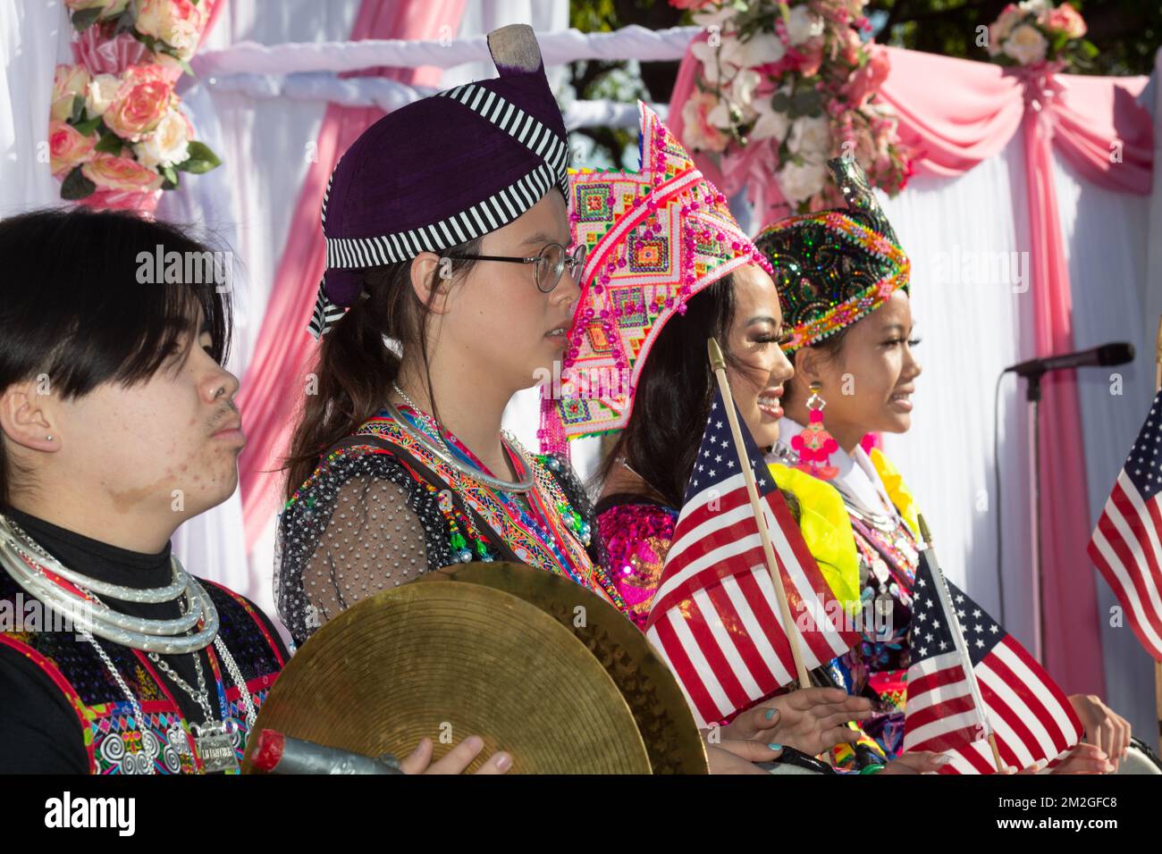 Hmong youth in traditional attire carry American flags in the entry ...