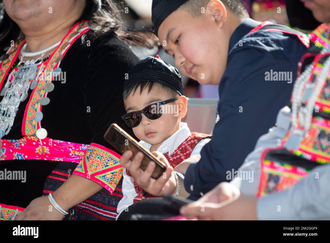 Young boy in sunglasses dressed in traditional Hmong attire looks at ...
