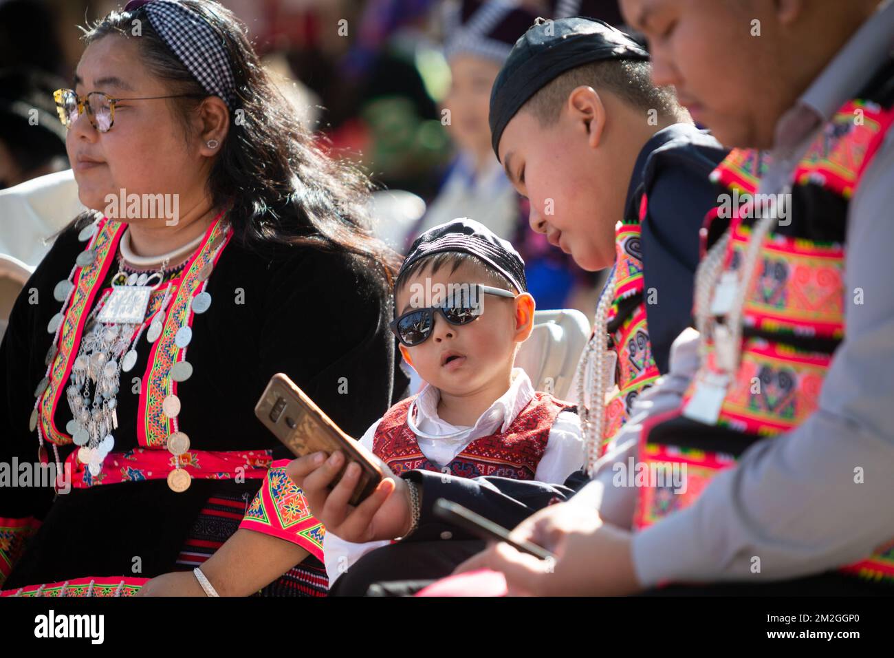 Young boy in sunglasses dressed in traditional Hmong attire looks at ...