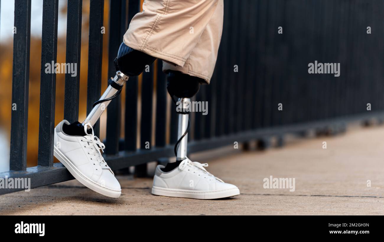 View of a man with prosthetic legs and white sneakers. Rested one foot ...