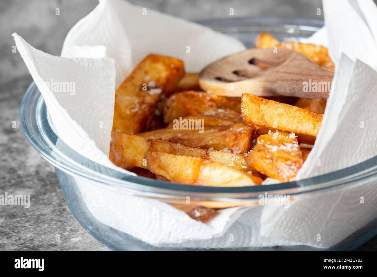 Homemade chips in a glass dish with a paper towel and wooden spoon. On ...