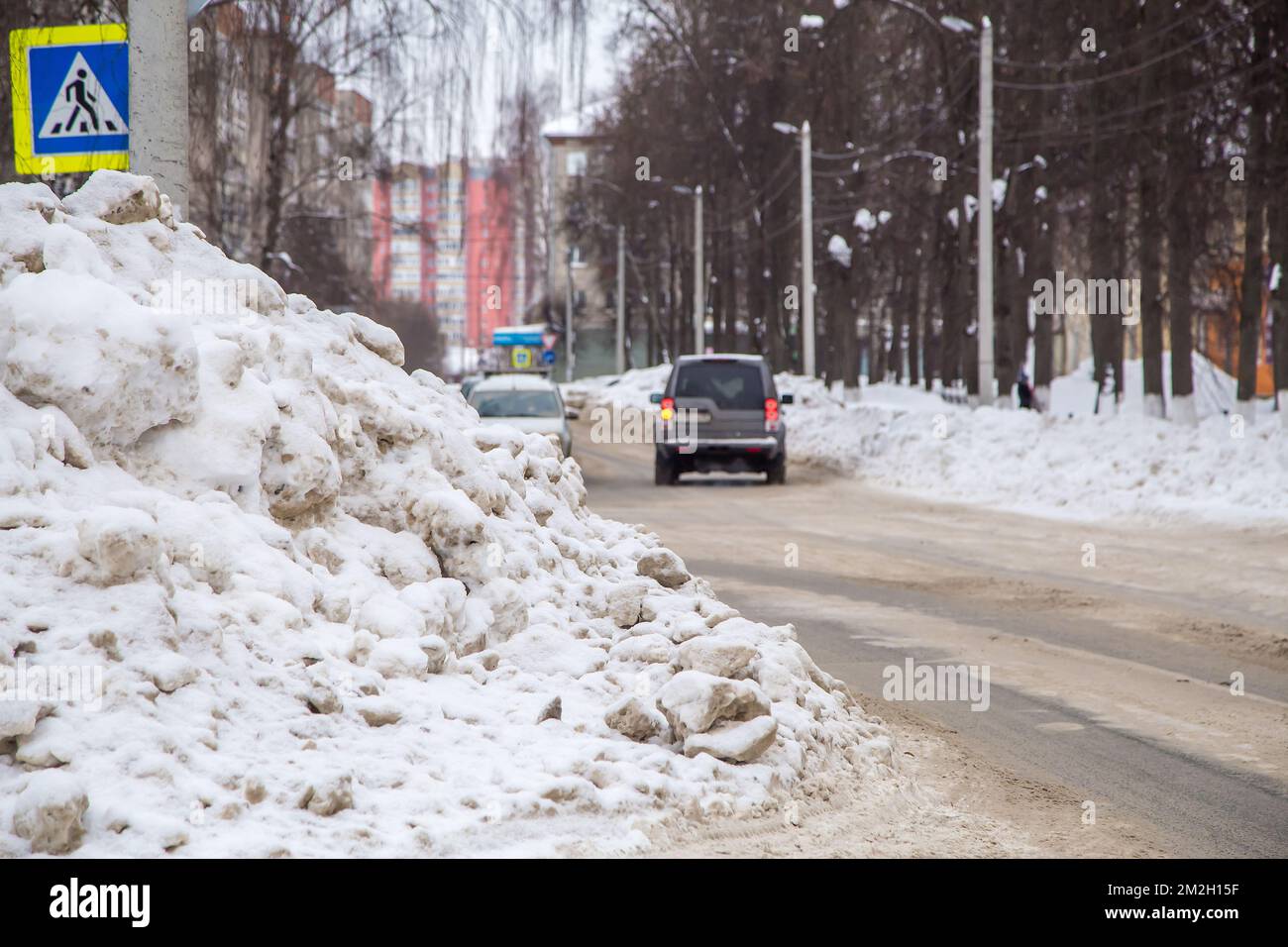 A large, high snowdrift against the backdrop of a city street with cars ...