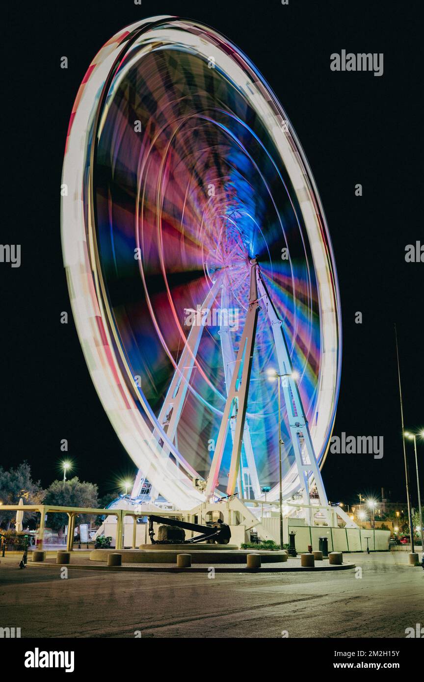 A vertical long exposure shot of a Ferris wheel at night with colorful ...