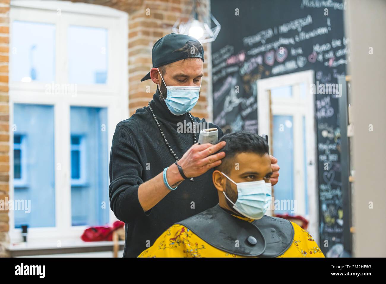 Hair and beard trimming during pandemic. Two adult man in a salon with ...