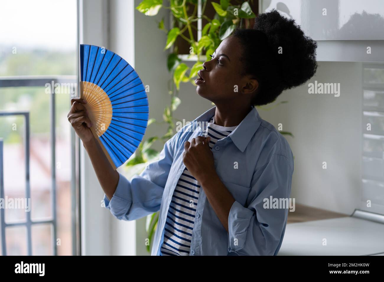 Young African American woman in blue shirt fanning herself with hand ...