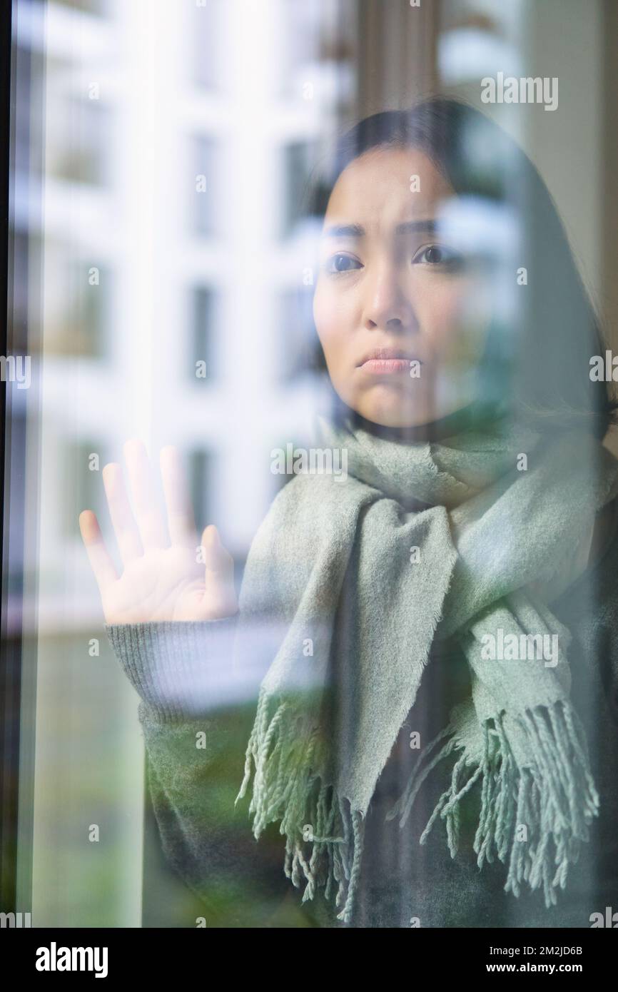 Asian woman feels unwell, stays at home, looks outside window with ...