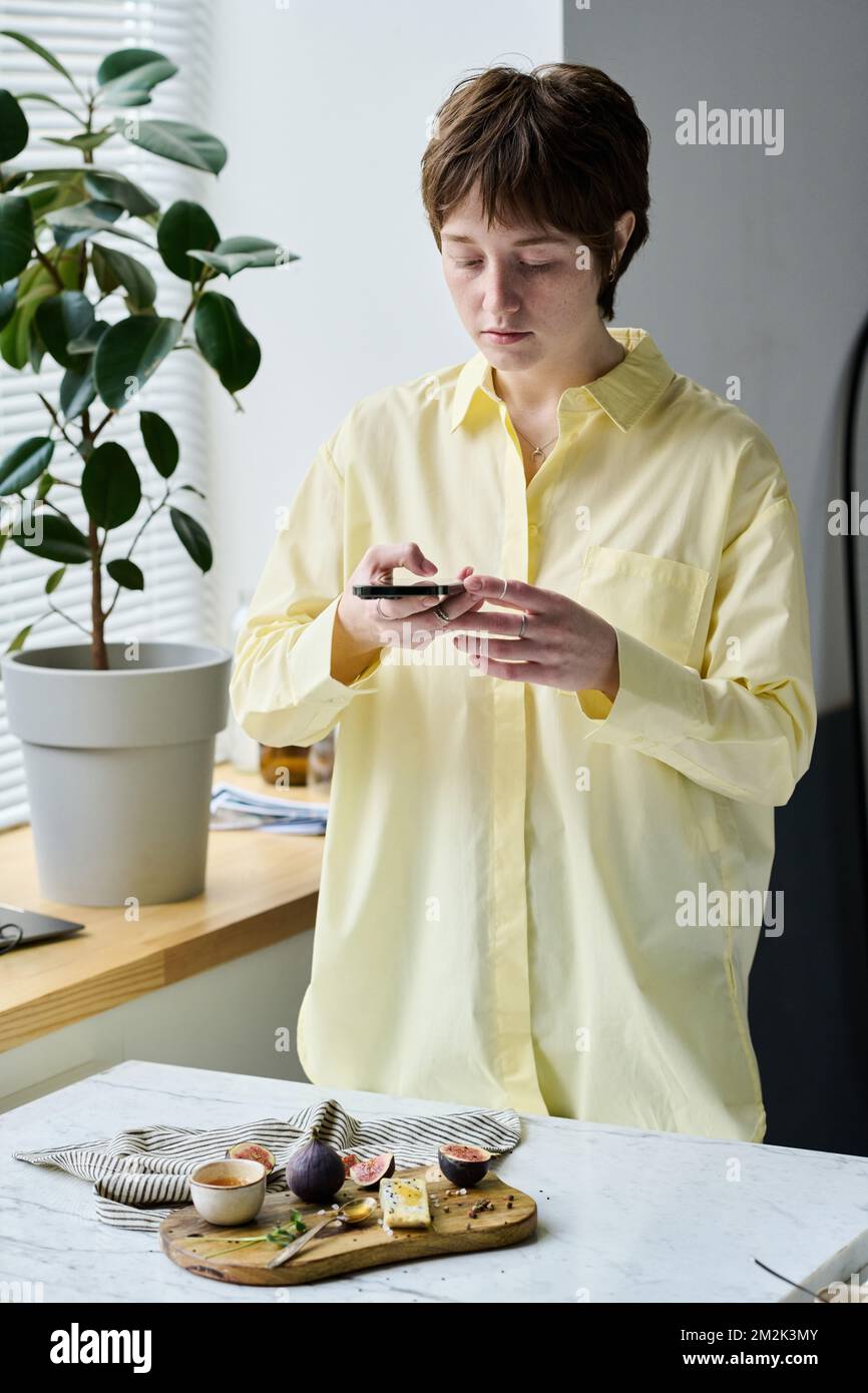Young photographer standing at table and photographing tray with food ...