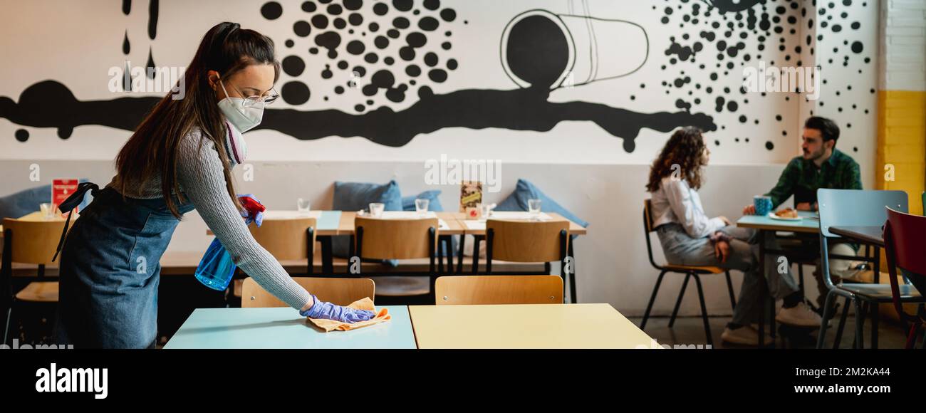 Horizontal banner side view waitress cleaning table in restaurant cafè ...