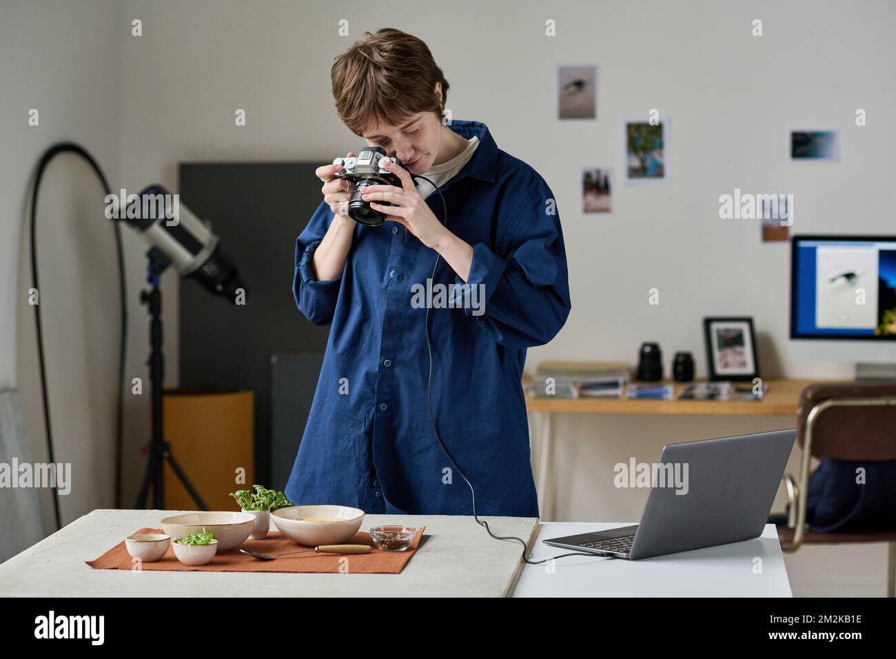 Young photographer connecting camera with laptop and taking pictures of ...