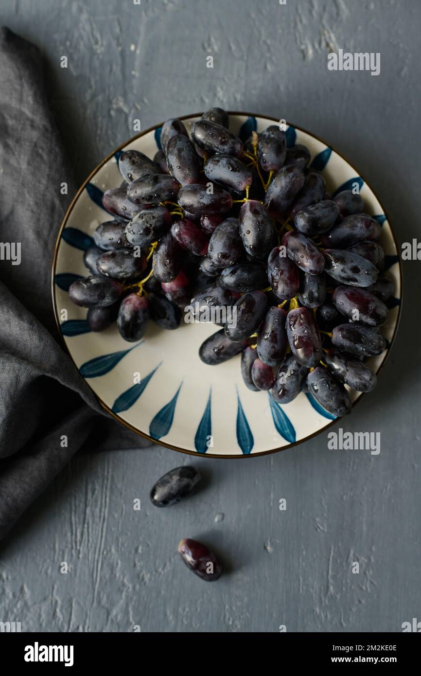 High angle view of bunch of ripe black grapes on plate on grey ...