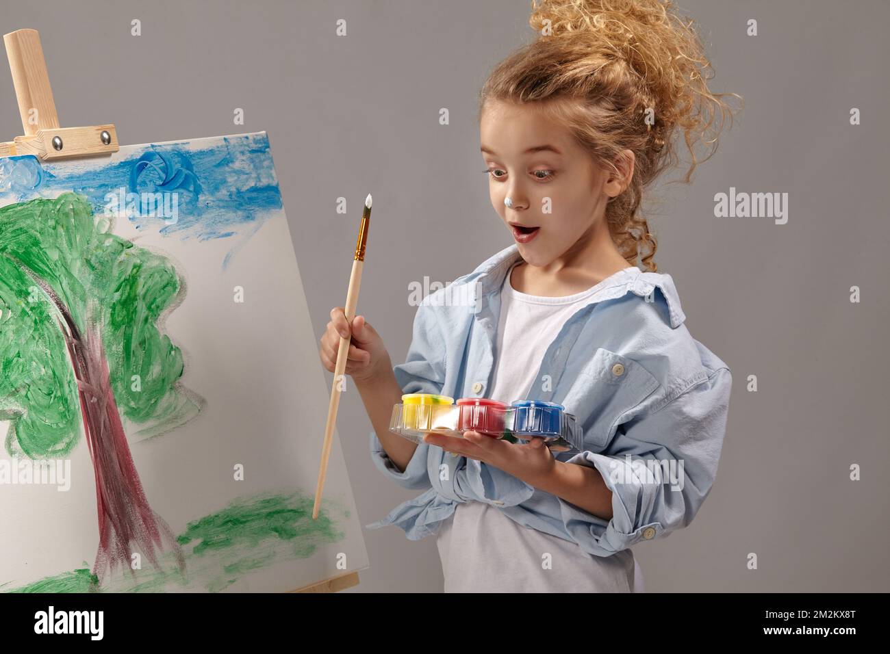 Charming school girl is painting with a watercolor brush on an easel ...