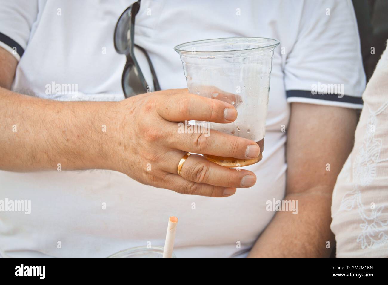 A closeup shot of a male's hand with a marriage ring and a plastic cup ...