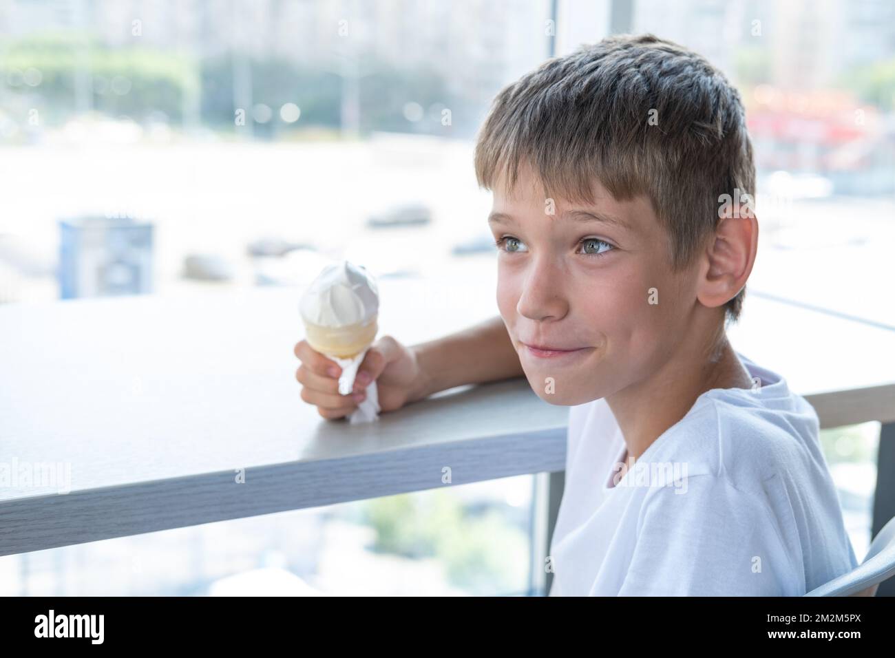 A cute teenage boy eats a swirling white ice cream in a waffle cup ...