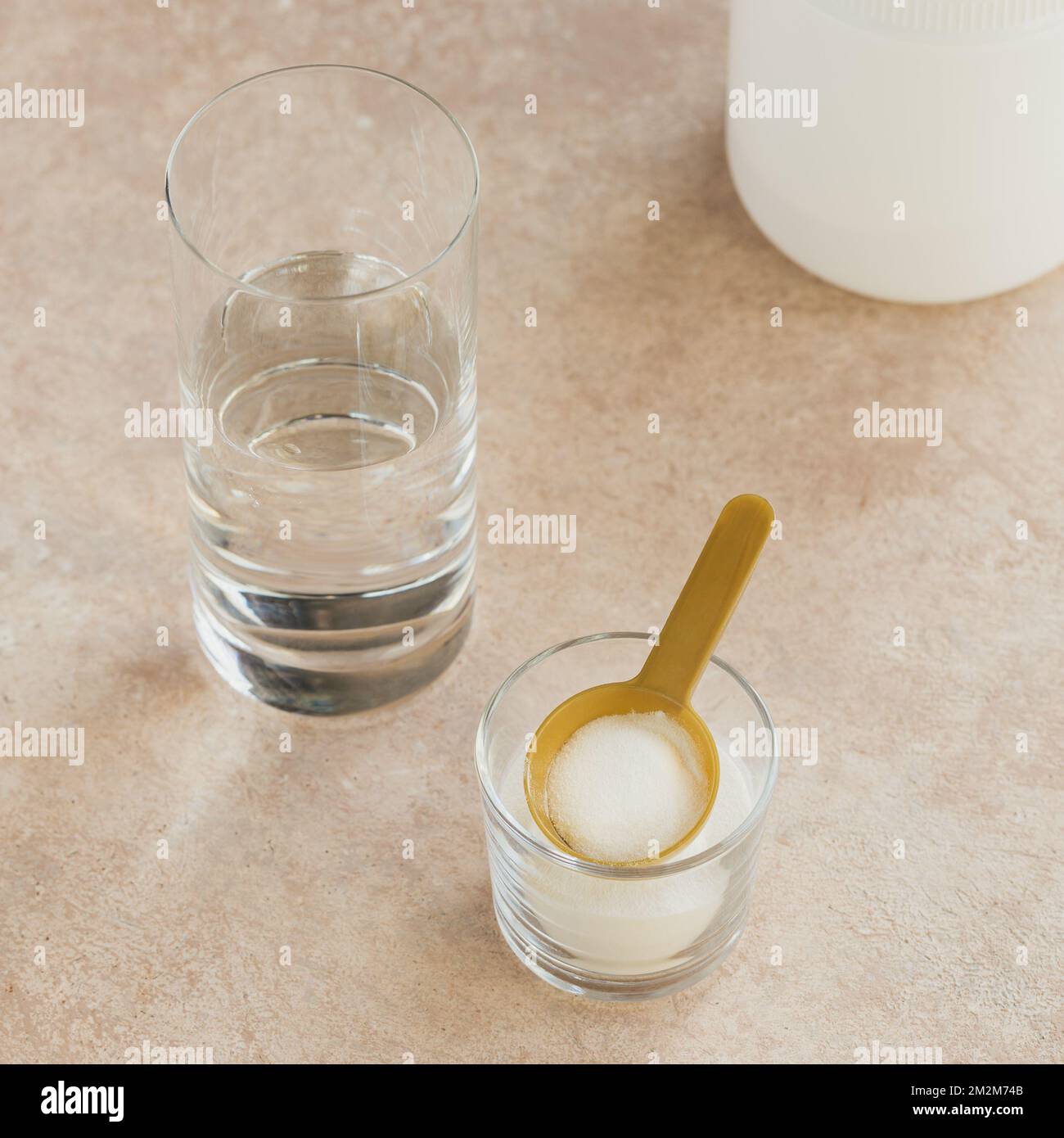 Collagen powder in bowl, glass of water and measure spoon on a light ...