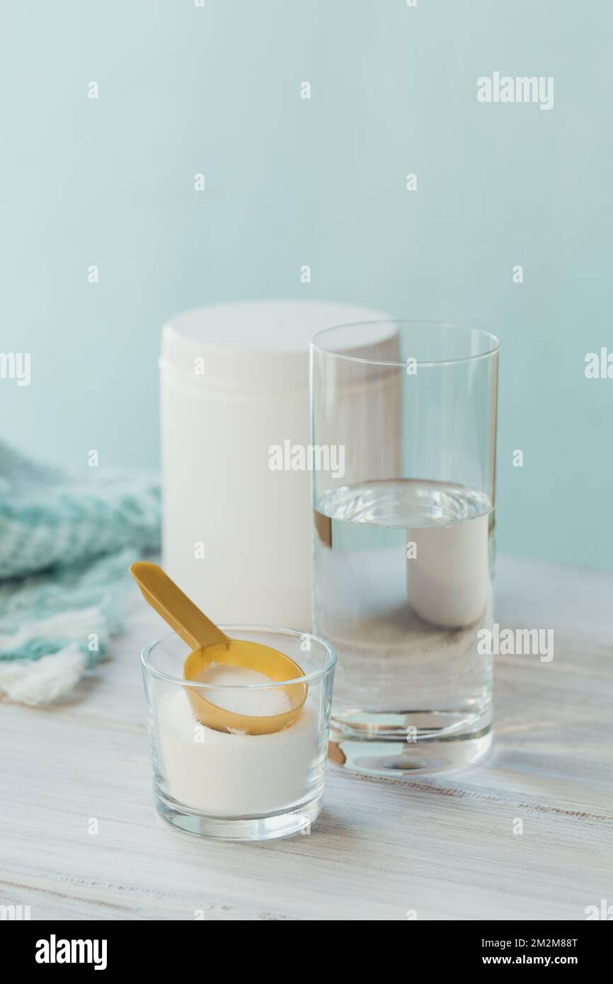 Collagen powder in bowl, glass of water and measure spoon on a on light ...